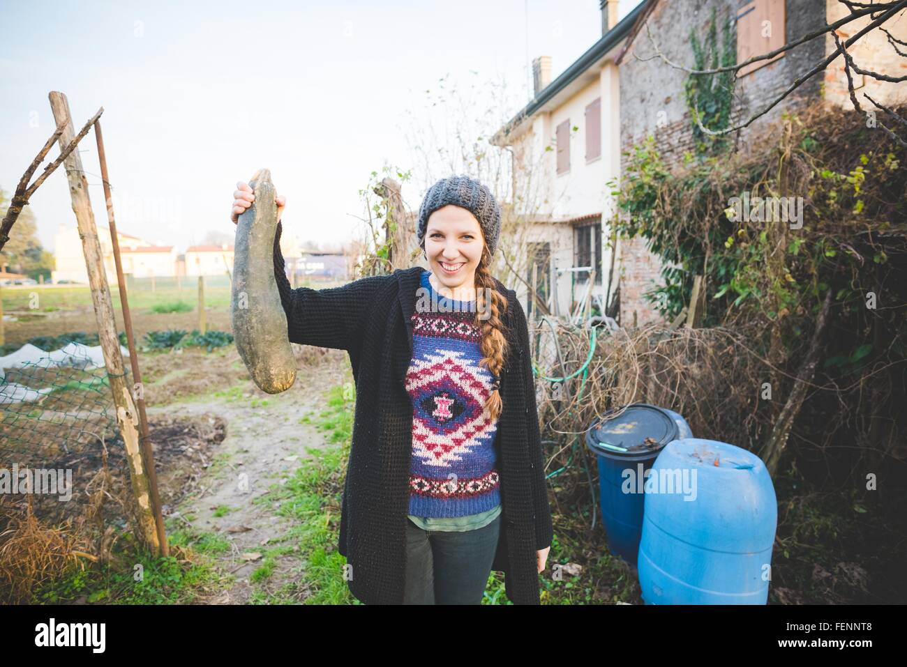 Young woman in garden holding marrow squash looking at camera smiling ...