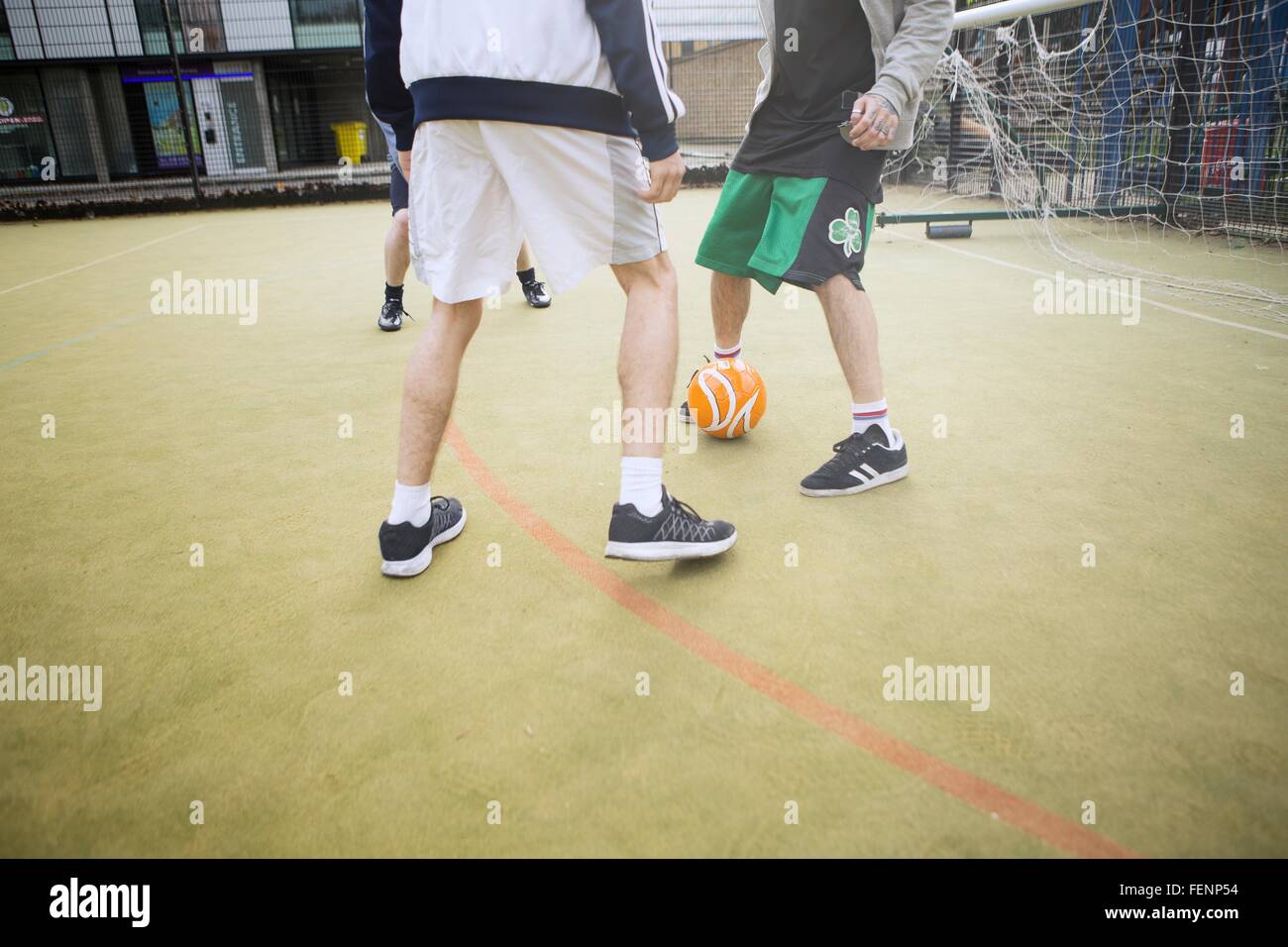 Group of adults playing football on urban football pitch, low section ...