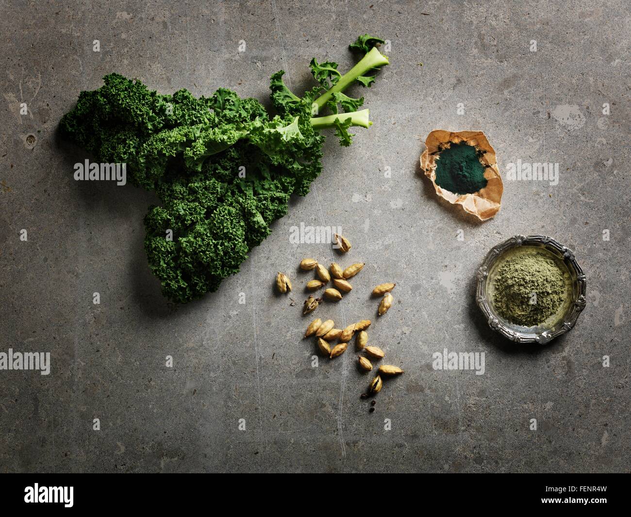 Overhead view of leafy vegetables, cardamom pods and ground supplements ...