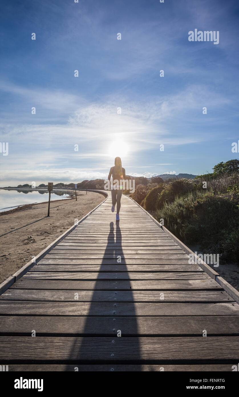 Female runner and her shadow running along beach boardwalk, Villasimius ...