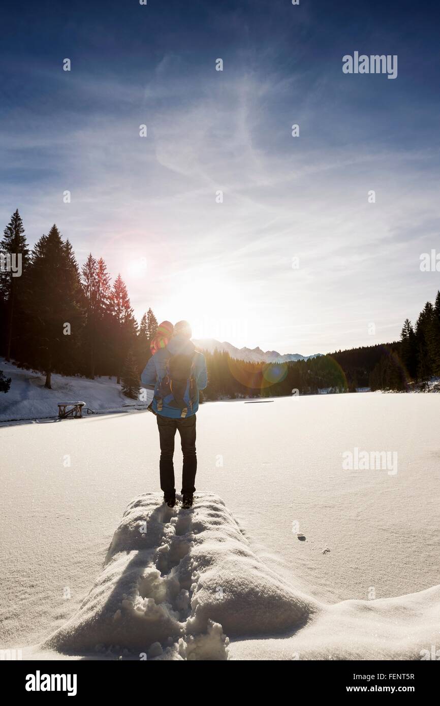 Rear view of man and toddler daughter looking out to snow covered lake ...