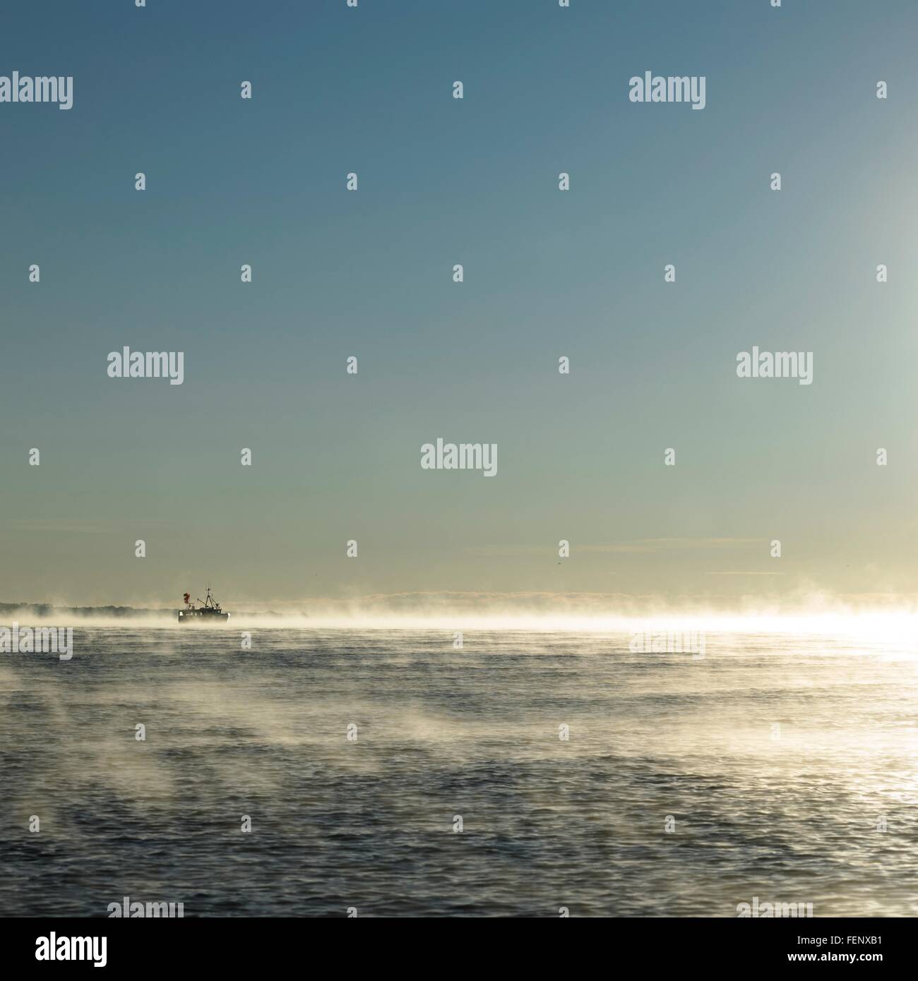Seascape with fishing boat on horizon in dawn sunlit mist Stock Photo ...