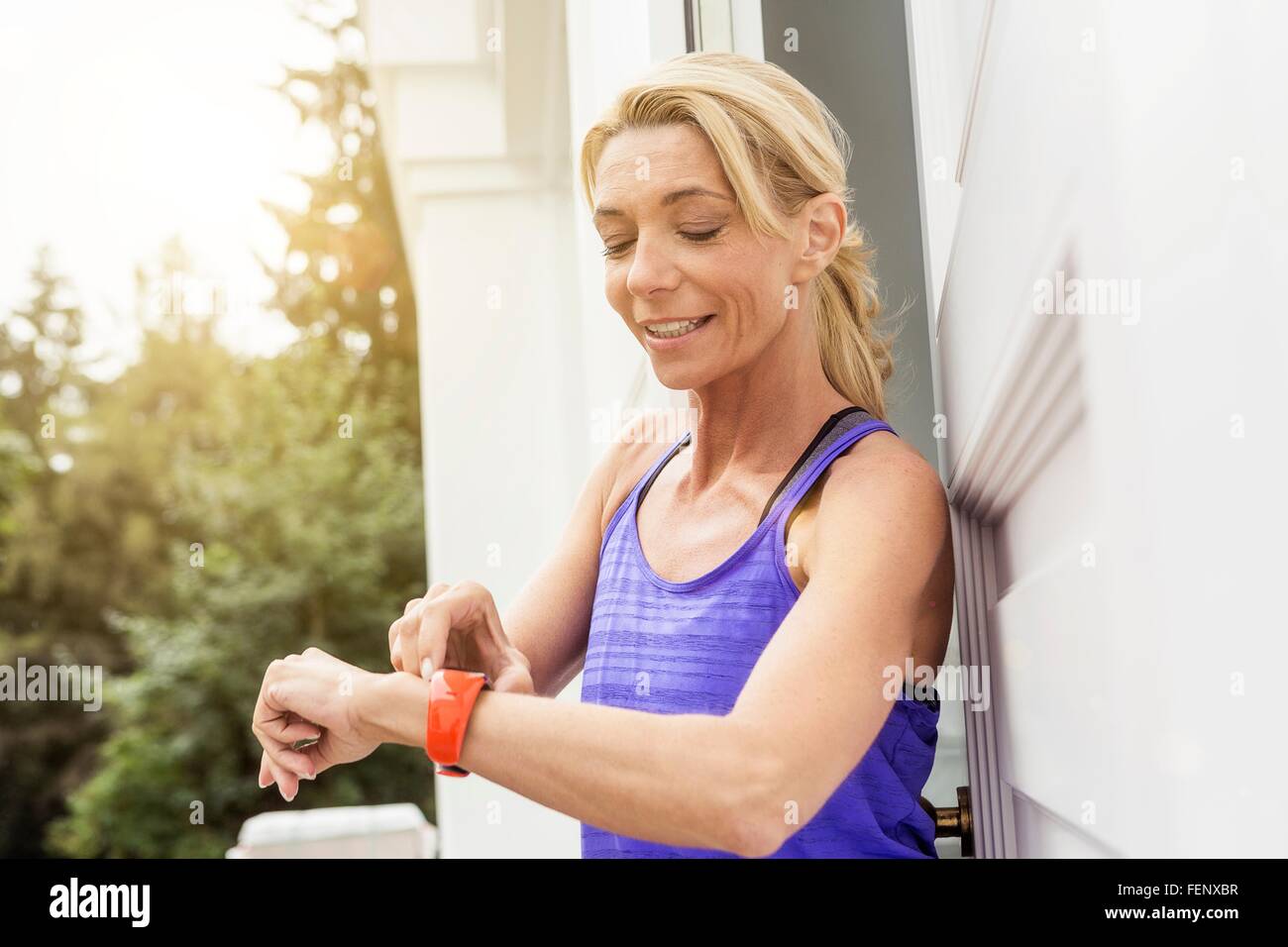 Mature female runner checking smartwatch at front door Stock Photo - Alamy