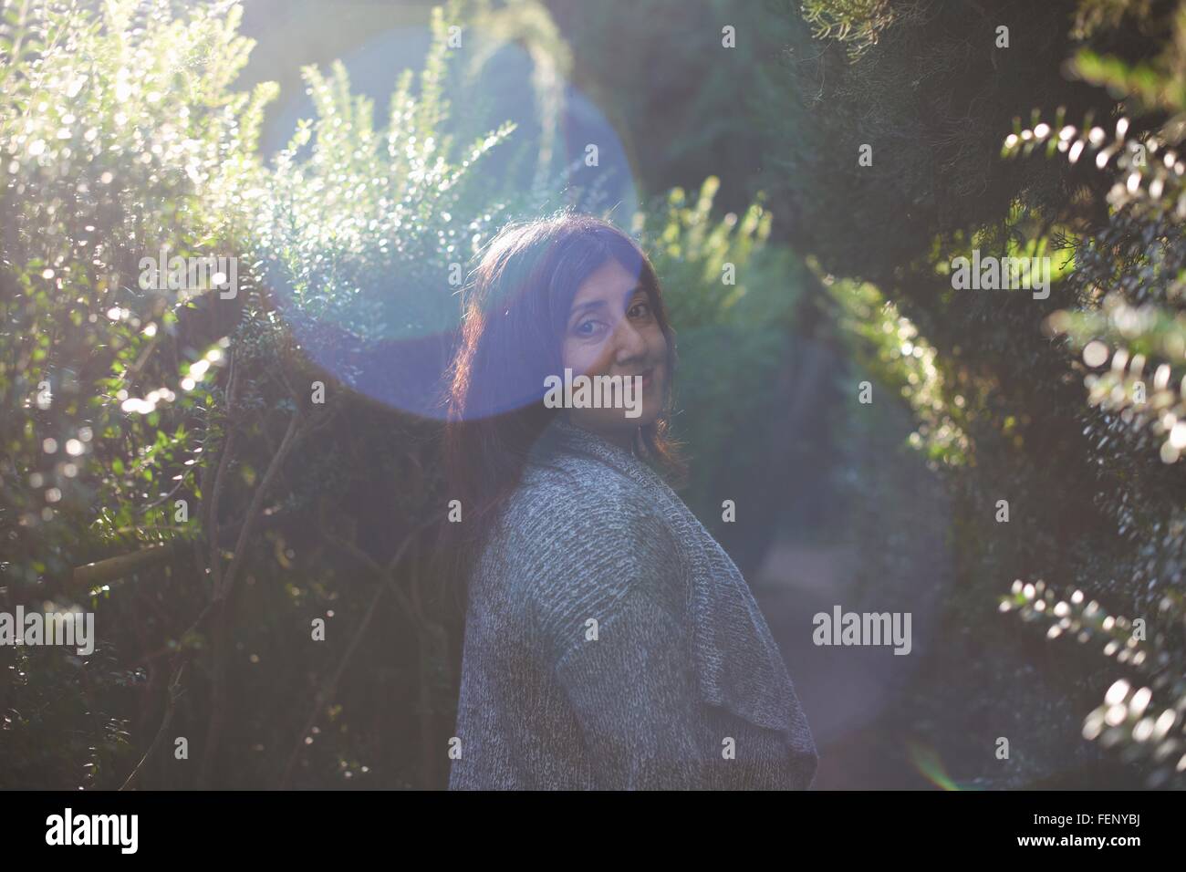 Mature woman wearing cardigan looking over shoulder at camera smiling ...