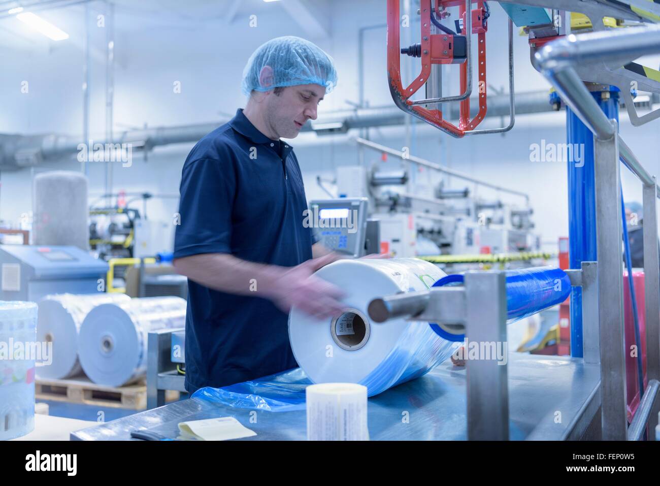 Worker moving roll of packaging in food packaging printing factory ...