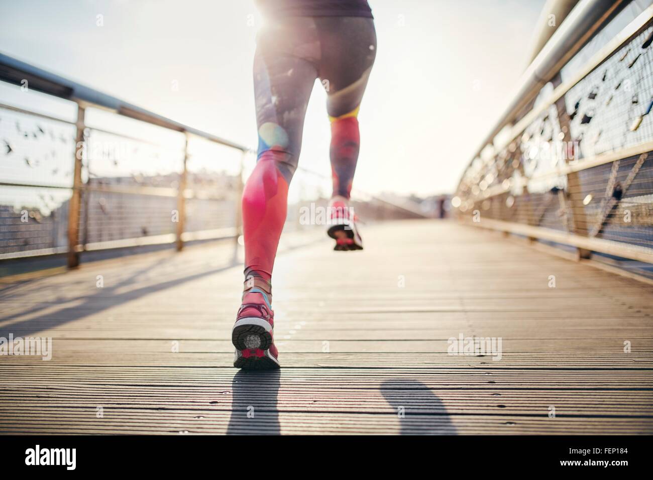 Rear waist down view of female runner running across footbridge Stock ...