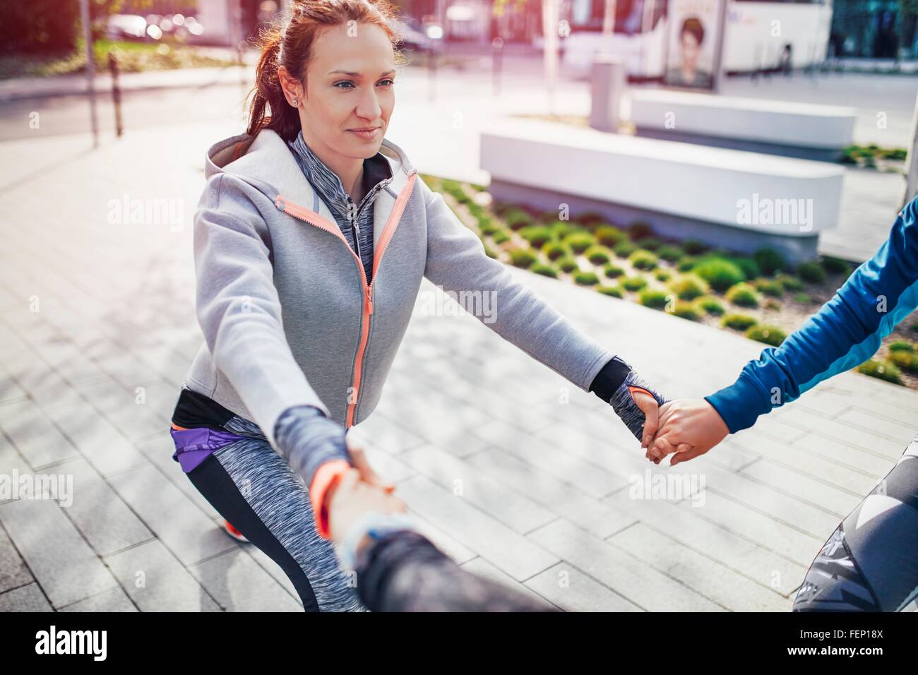 Three female runners holding hands whilst doing warm up exercises in ...
