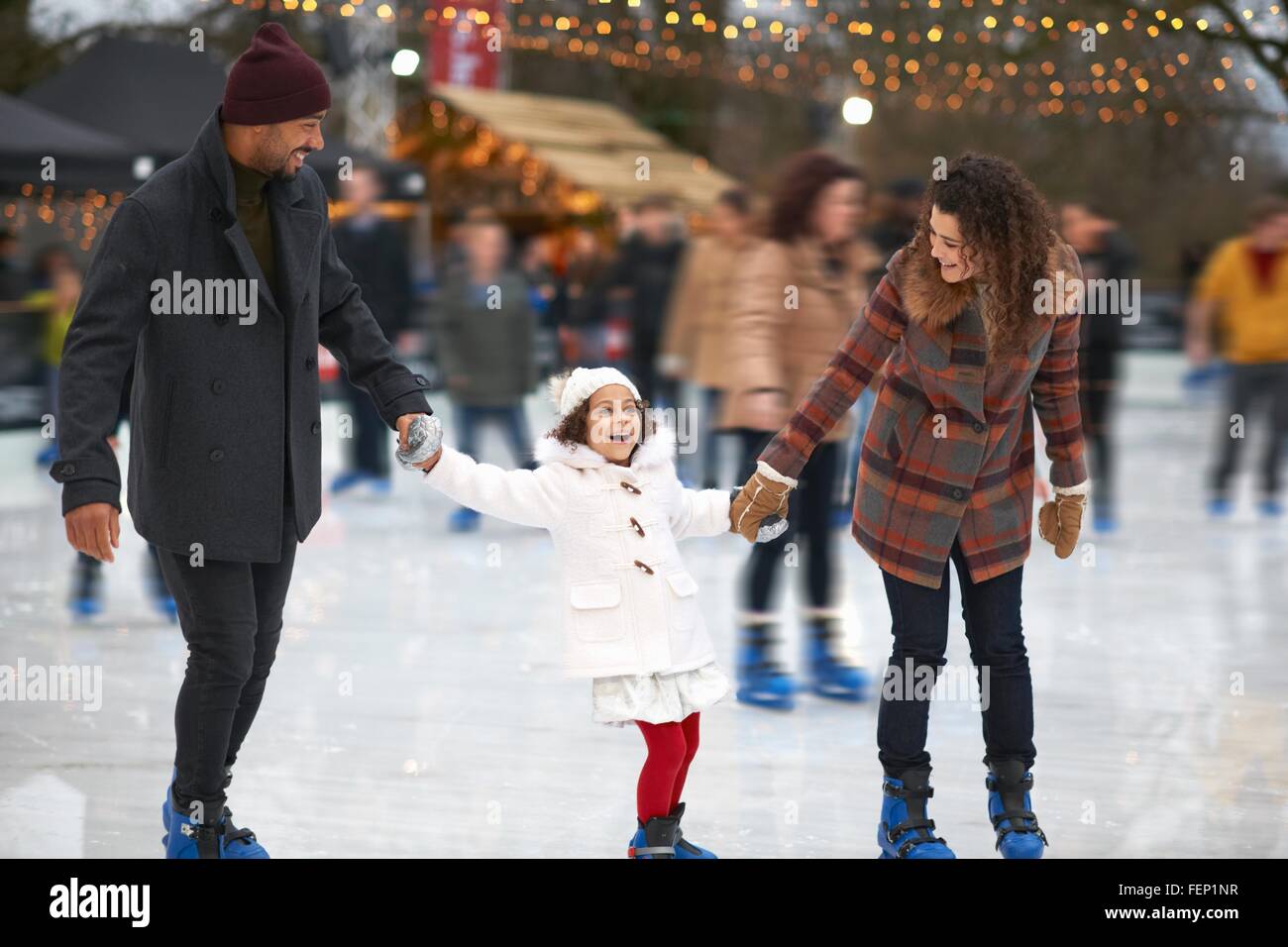 Girl holding parents hands ice skating, smiling Stock Photo - Alamy