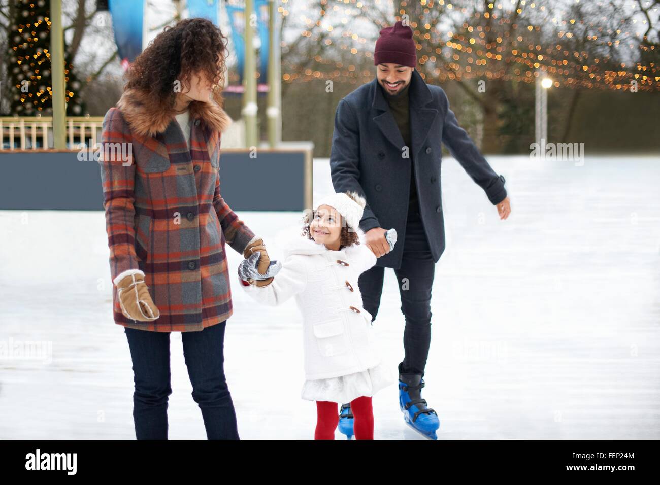 Girl ice skating, holding hands with parents looking up smiling Stock ...