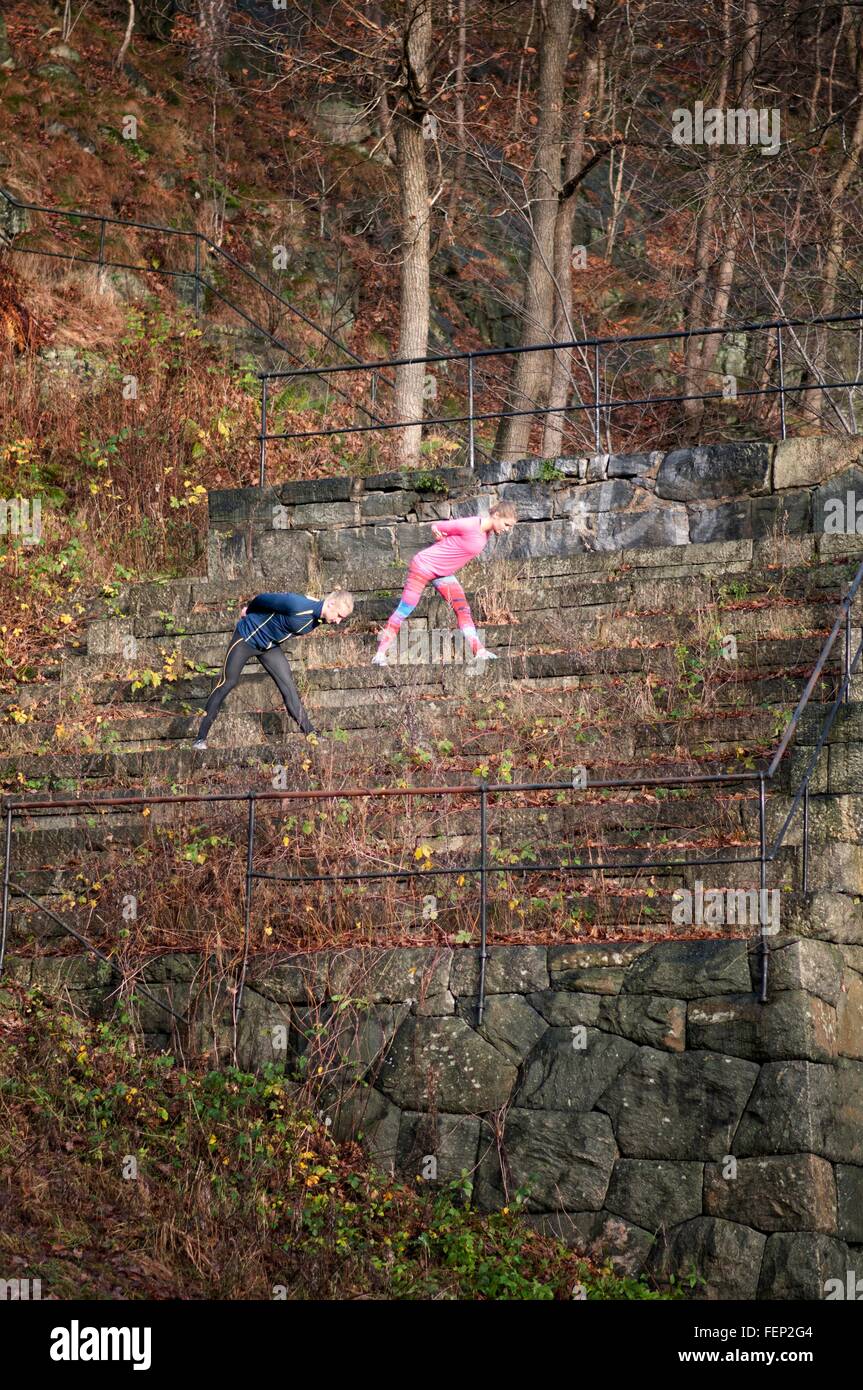 Side view of couple doing stretching exercises on overgrown stone steps ...