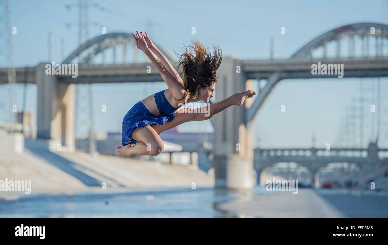 Side view of dancer jumping in mid air in front of bridge, Los Angeles ...