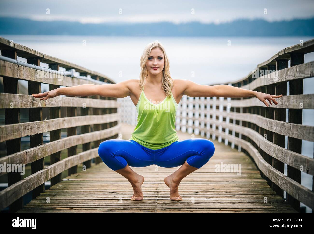 Portrait of young woman crouching in yoga pose on wooden pier Stock ...