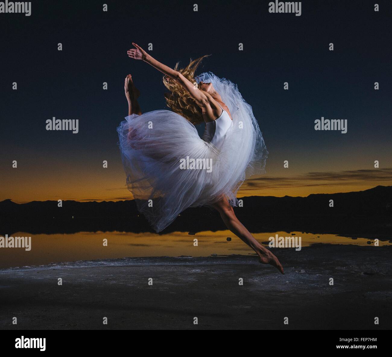Young female ballet dancer leaping over Bonneville Salt Flats at dusk ...
