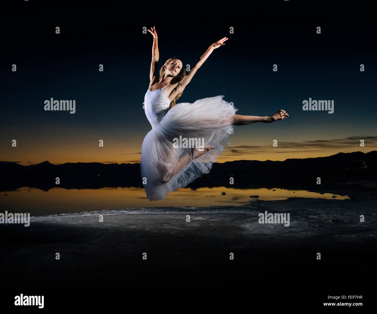 Young female ballet dancer leaping over Bonneville Salt Flats at sunset ...