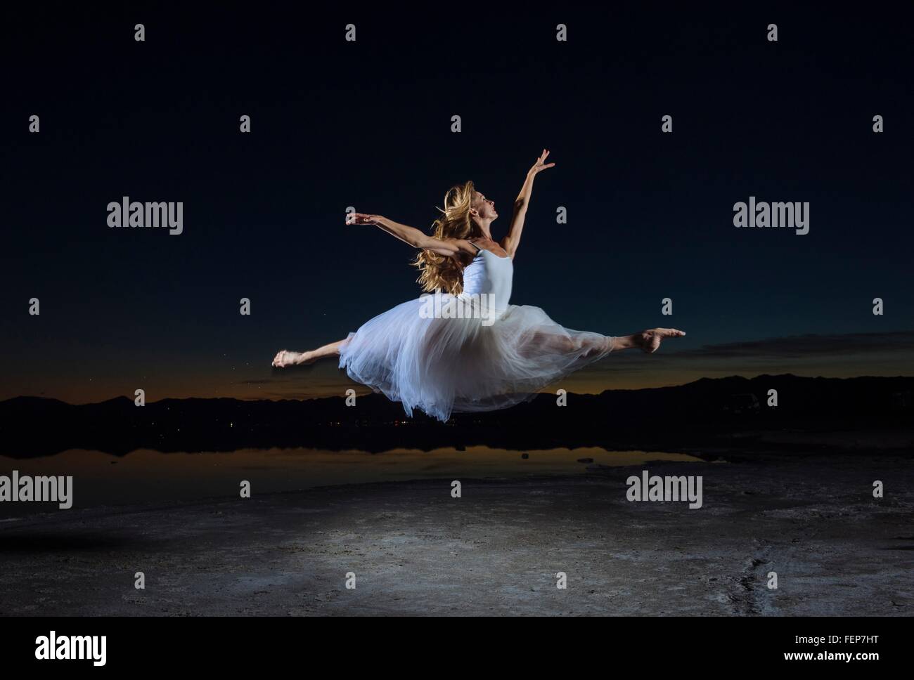 Young female ballet dancer leaping over Bonneville Salt Flats at night ...