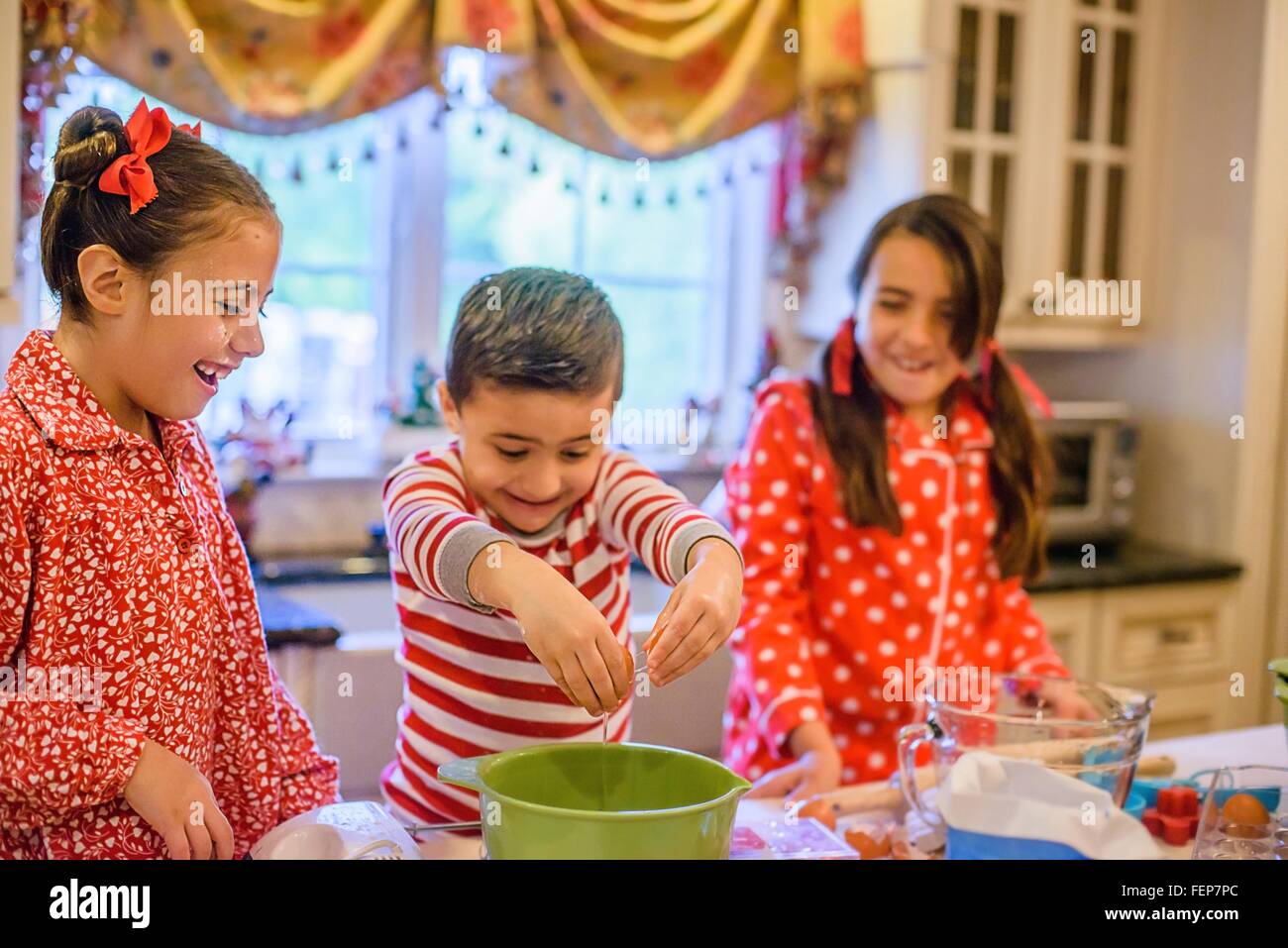 Children in kitchen wearing pyjamas cracking eggs into mixing bowl ...