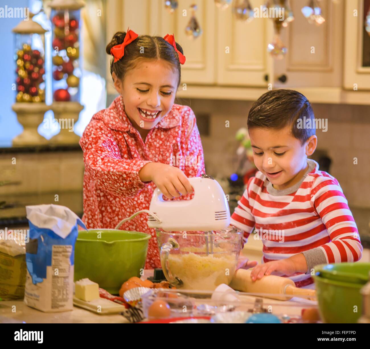 Children in kitchen wearing pyjamas using hand mixer on cookie dough ...