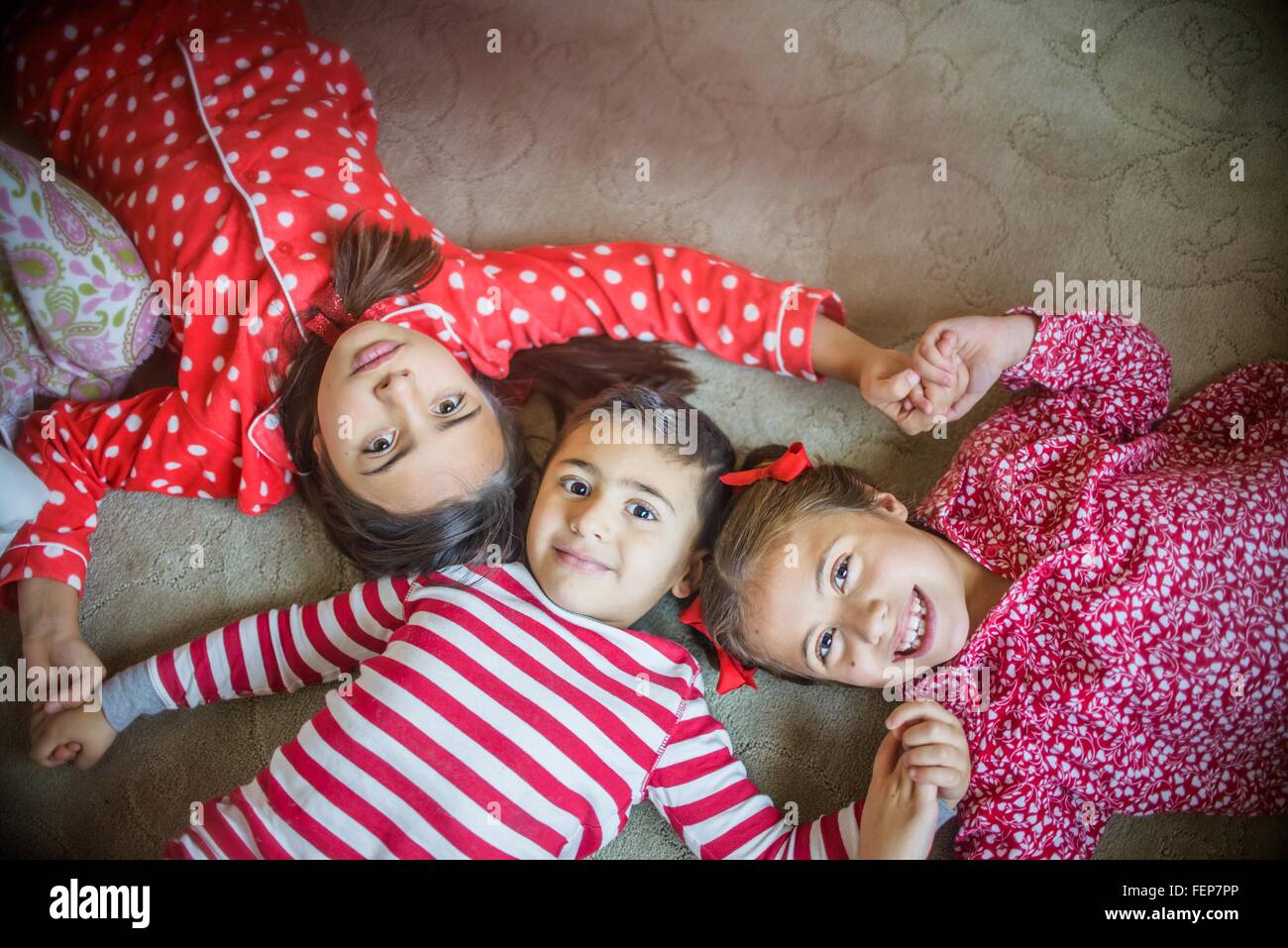 Overhead view of children wearing pyjamas lying on carpet looking at ...