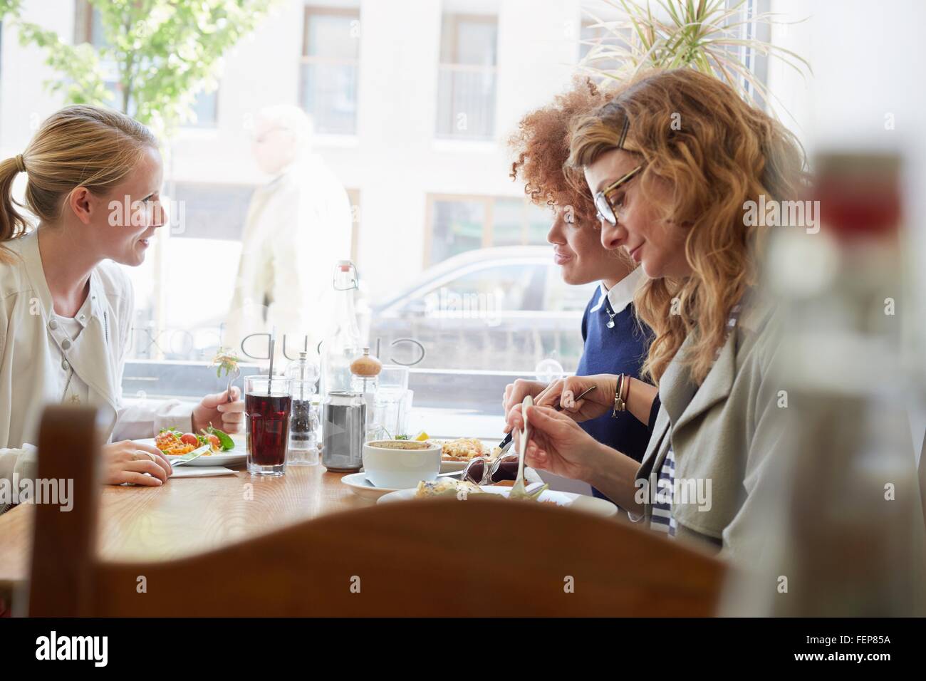 Three female friends eating lunch in cafe Stock Photo - Alamy