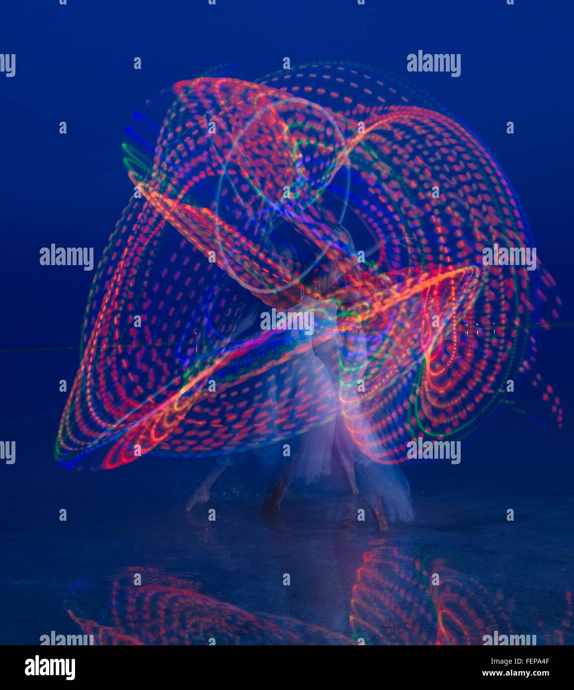 Woman dancing and swirling illuminated multi-coloured hoop at dusk ...