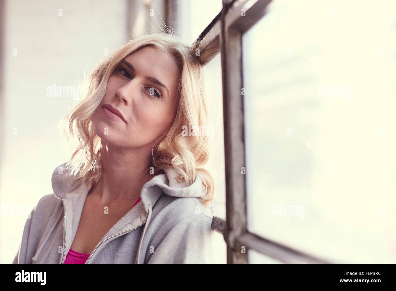 Portrait of blond mid adult woman leaning against window Stock Photo ...