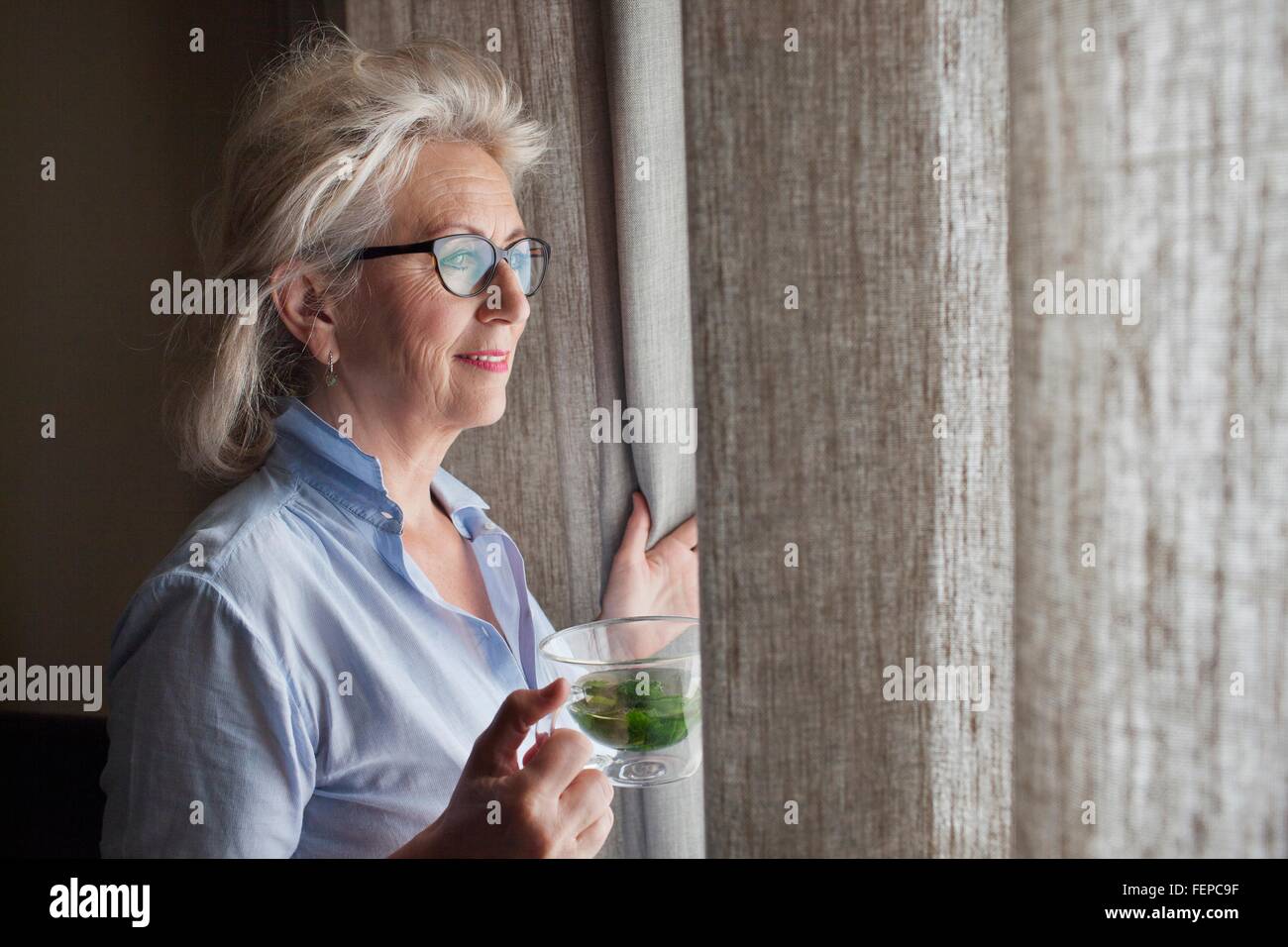 Senior woman holding drink, looking out of window Stock Photo - Alamy
