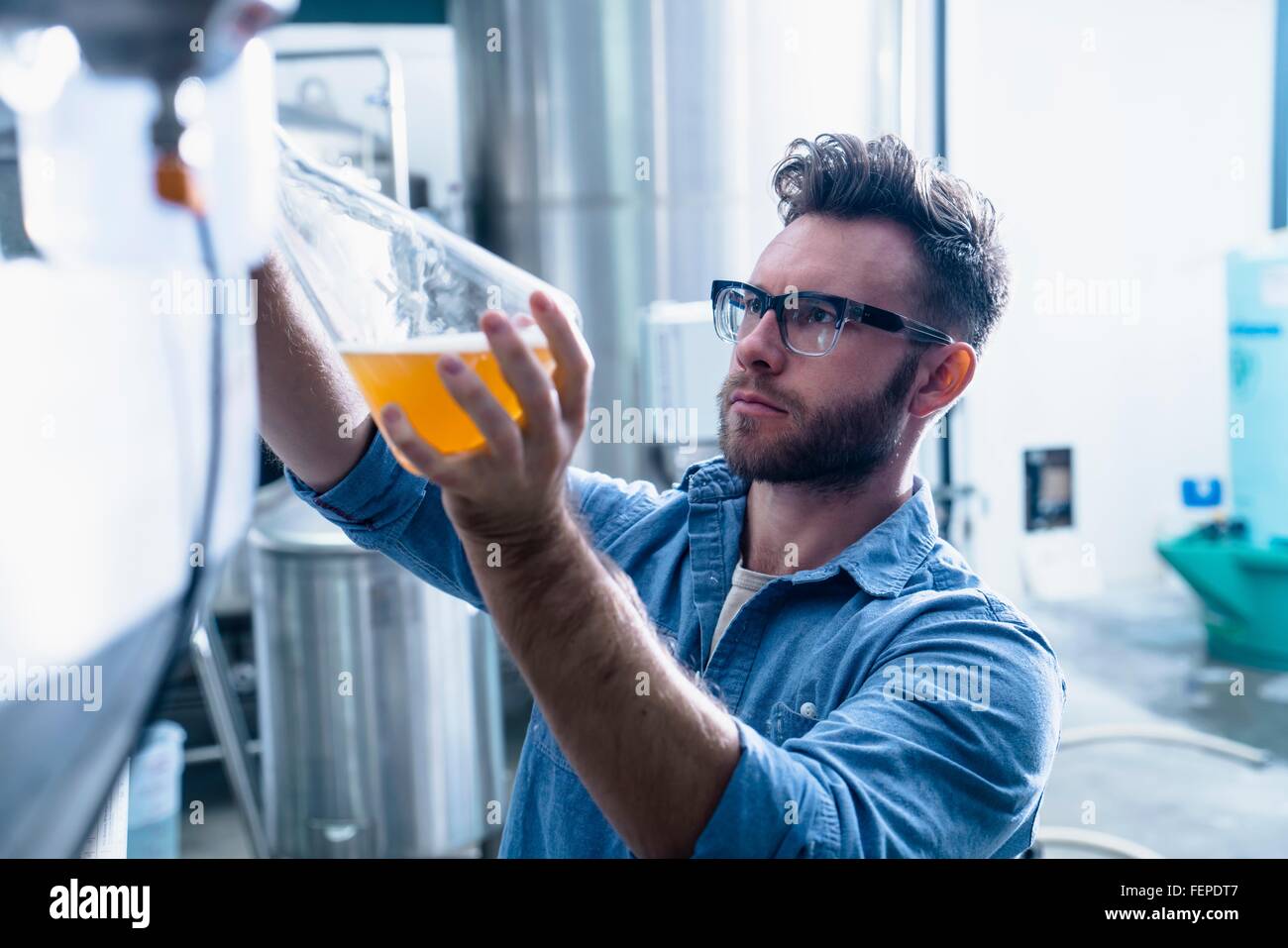 Young man in brewery filling flask with beer Stock Photo - Alamy