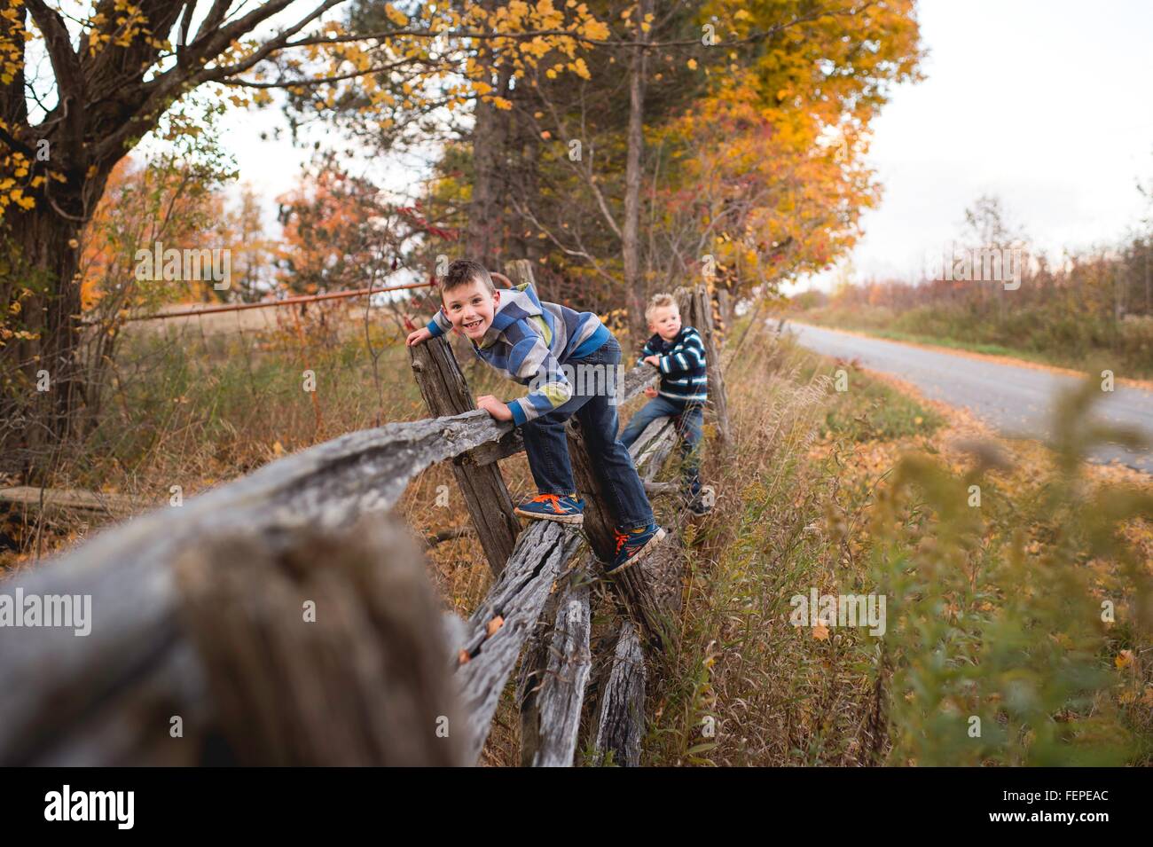Boys climbing over fence looking at camera smiling Stock Photo - Alamy