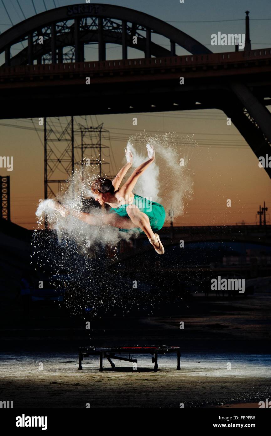 Female ballet dancer leaping whilst releasing powder explosion above ...