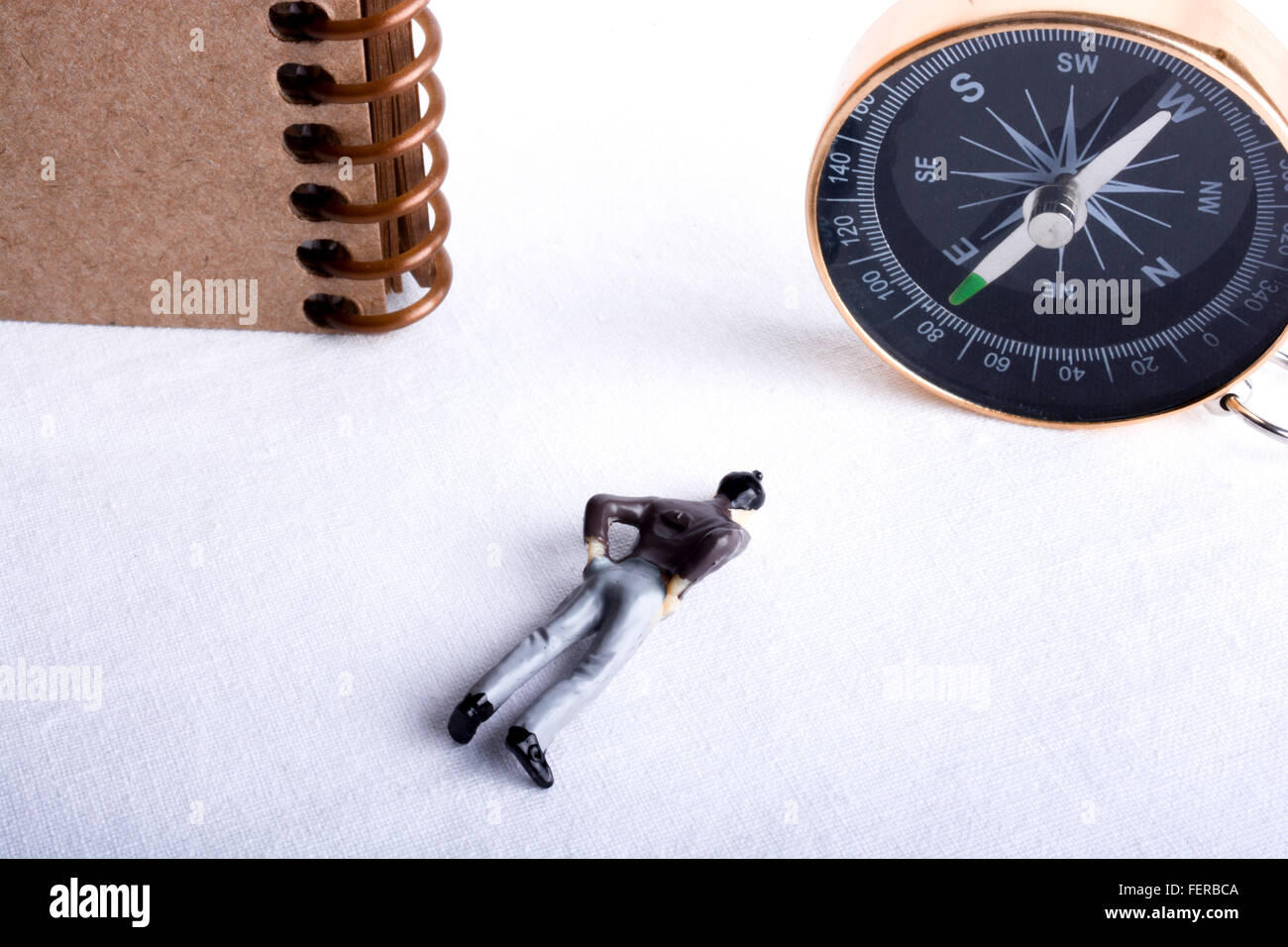 Man lying down by the side of a compass and spiral notebook on a white ...