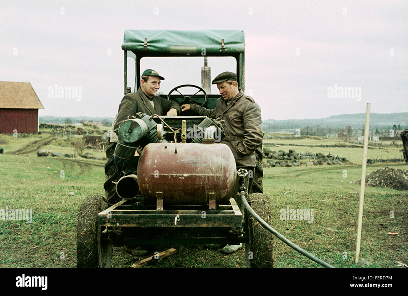 Two men operating a tractor with a compressor in Höggum, Västergötland ...
