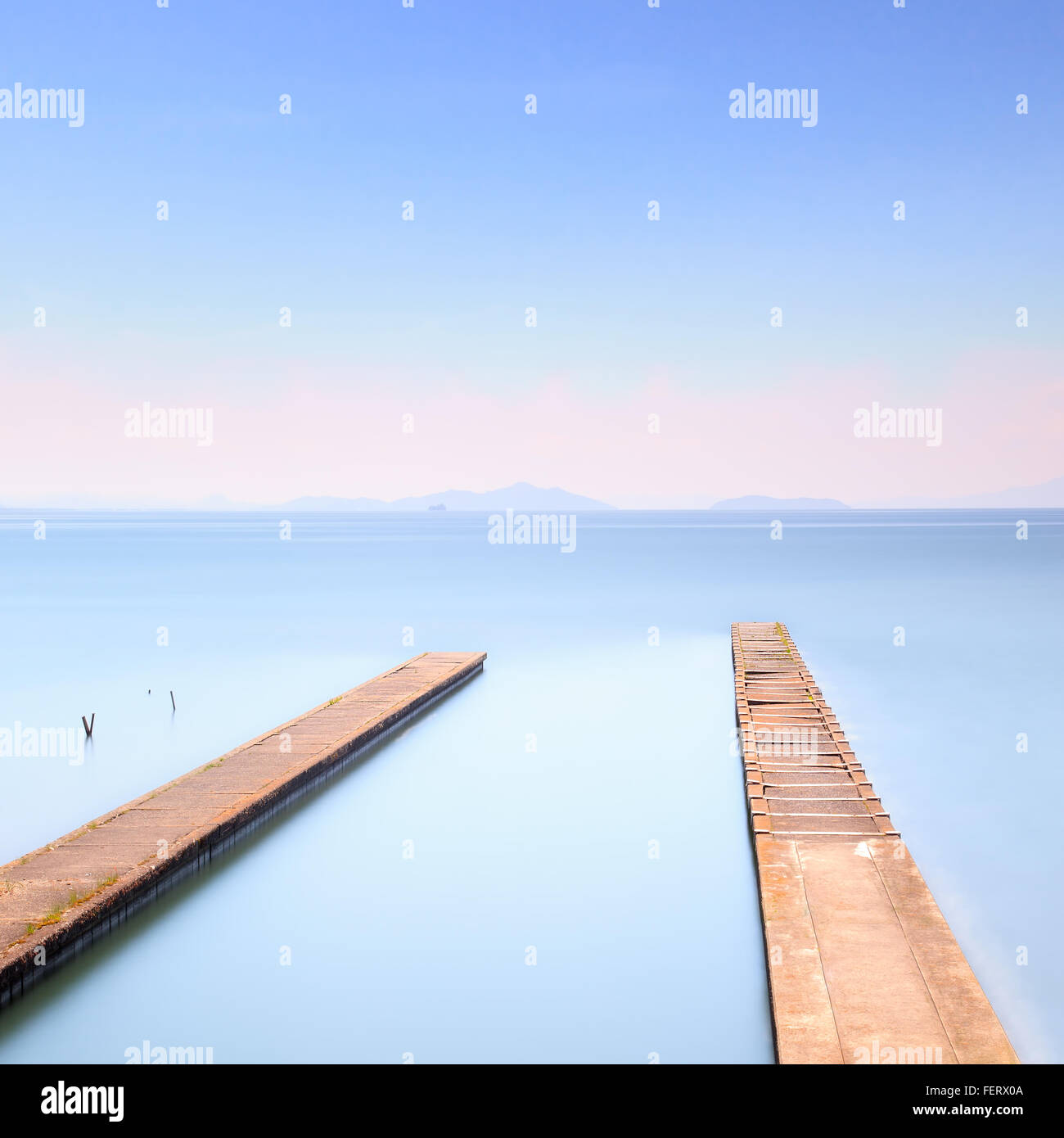 Two concrete pier or jetty on a blue sea. Hills on background. Long ...