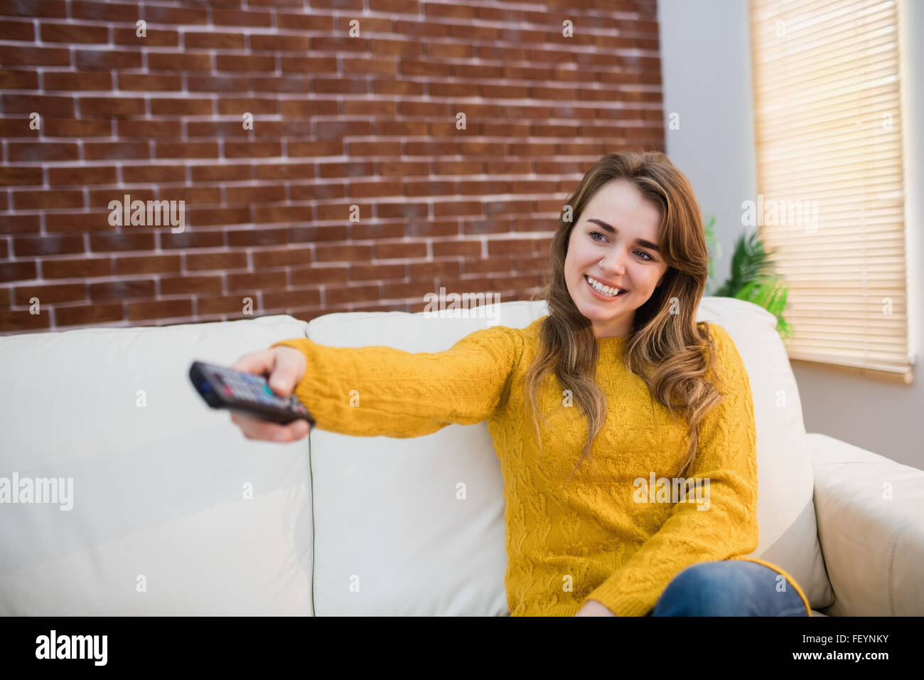 Smiling woman holding remote control on couch Stock Photo - Alamy