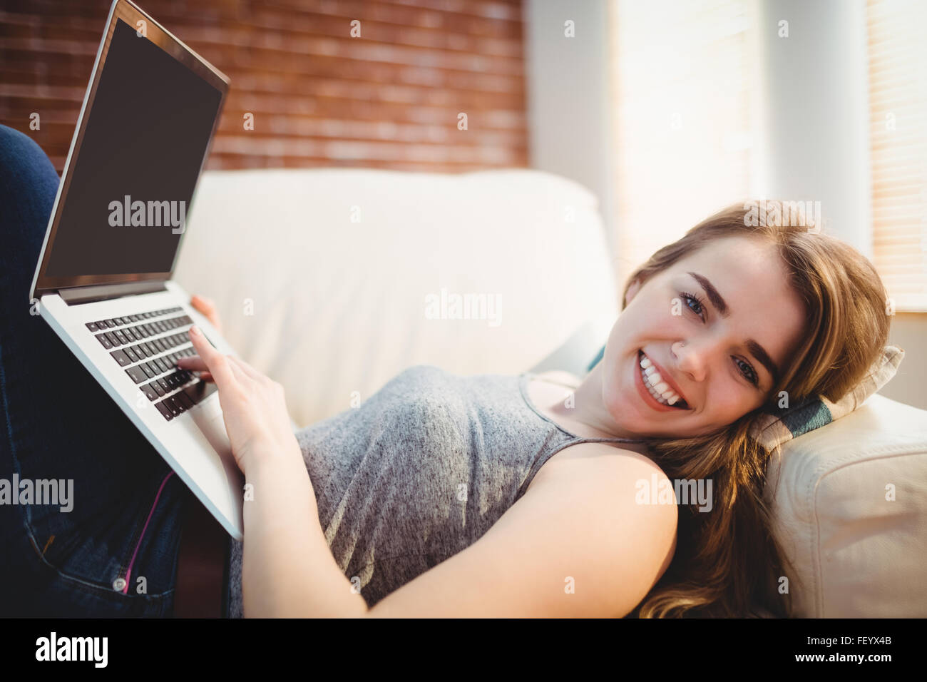 Pretty woman lying on the couch using her laptop Stock Photo - Alamy