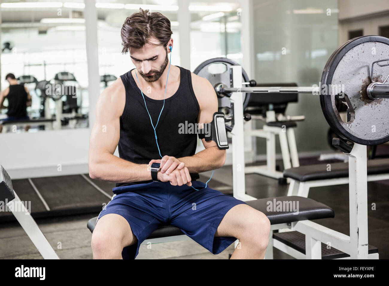 Muscular man sitting on barbell bench and using smartwatch Stock Photo ...
