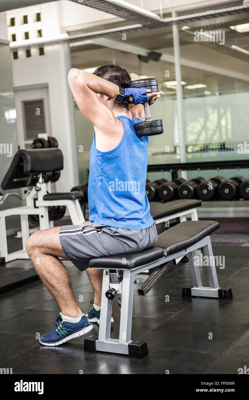 Muscular man lifting dumbbell while sitting on bench Stock Photo - Alamy
