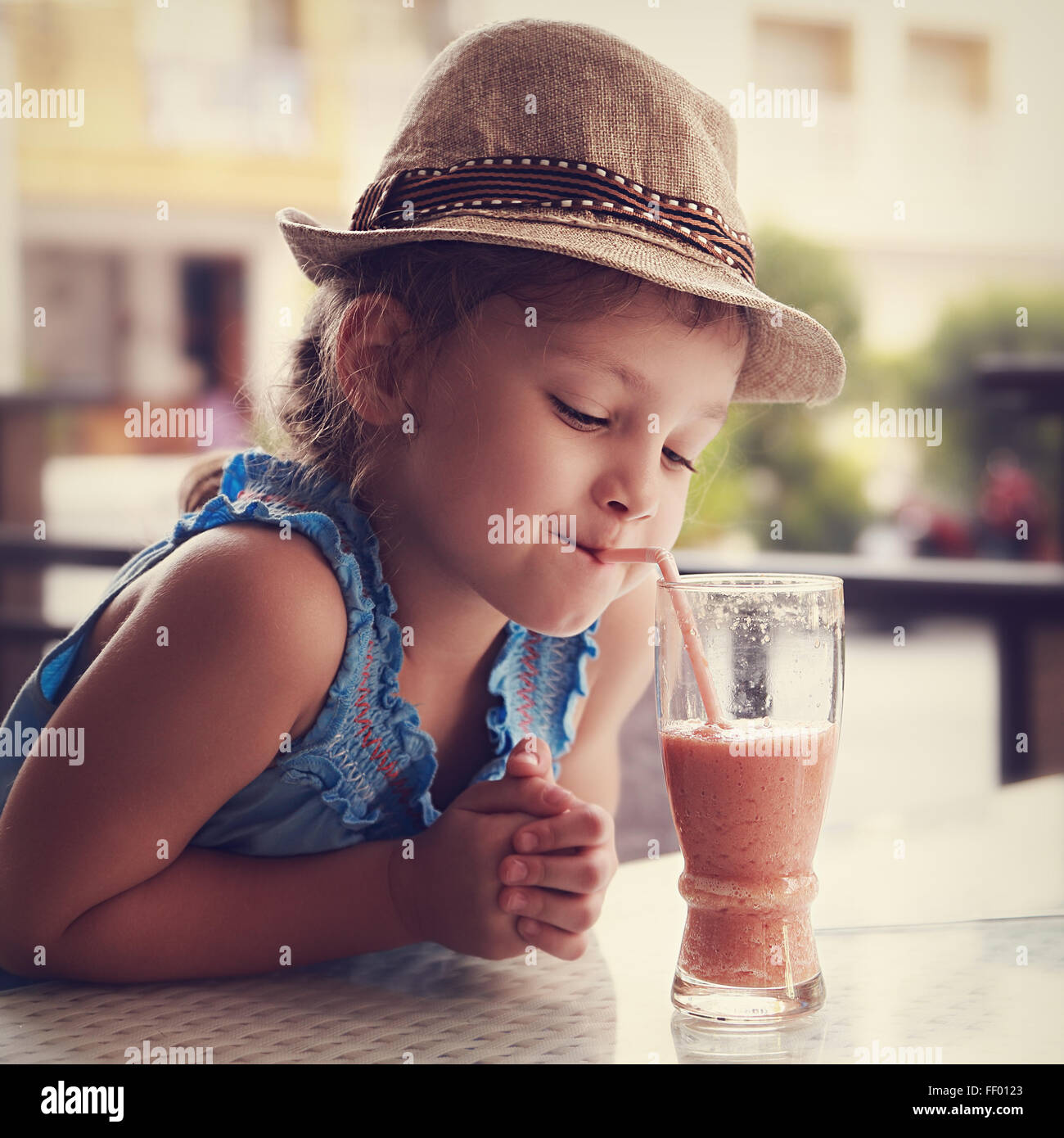 Cute thinking kid girl drinking tasty juice in street restaurant. Toned ...