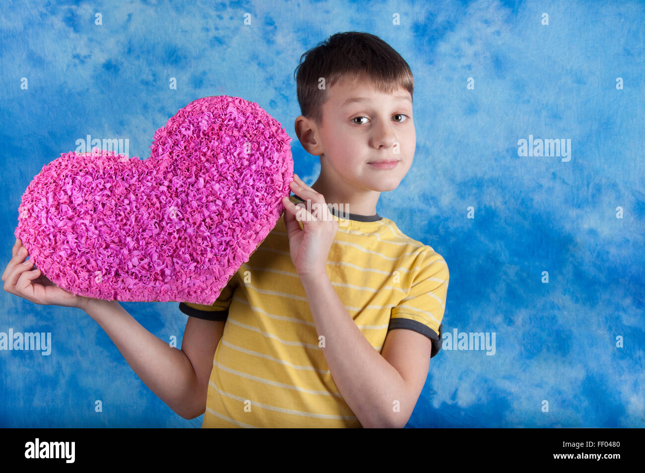 Cute young boy holding pink paper heart in his hands on blue background ...