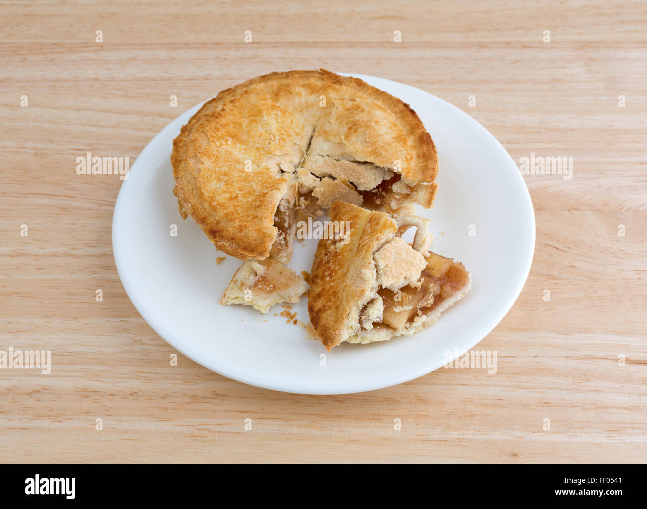 A small apple pie with a piece broken off on a plate atop a wood table ...