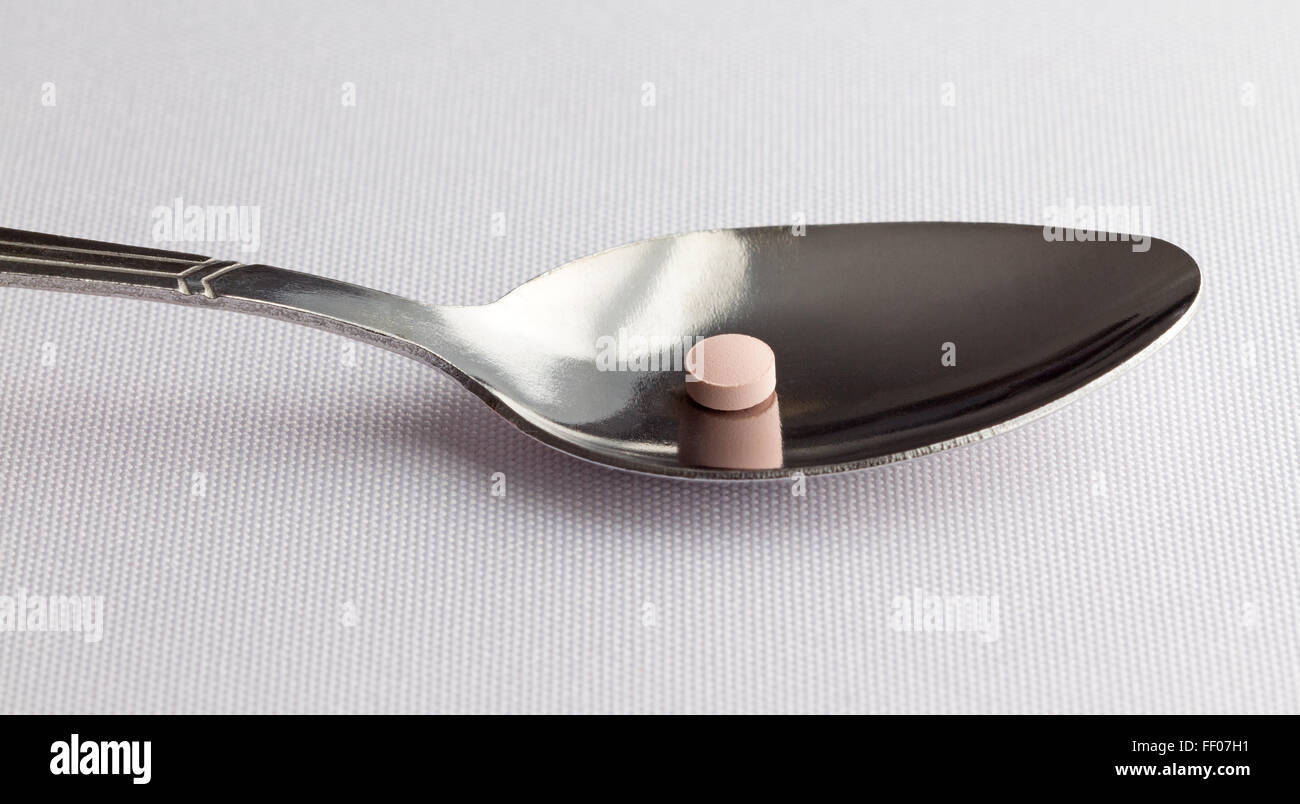 A single famotidine tablet on a spoon upon an off white table cloth ...