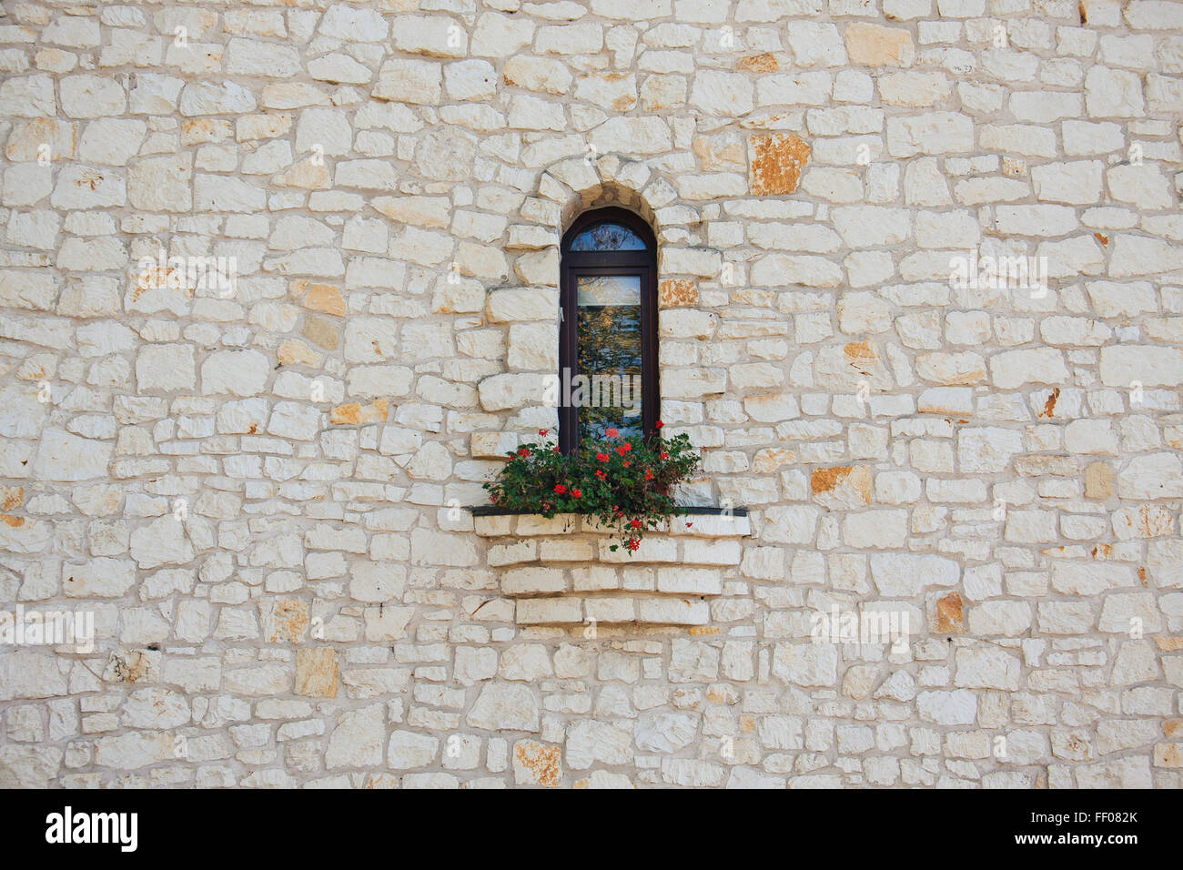 A white stone wall with a flower box in the window, adding charm to the ...