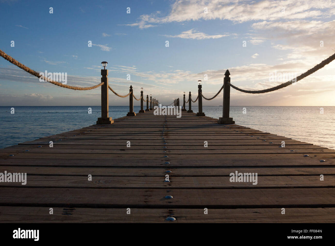 A wooden boardwalk with rope railing stretches out over the ocean ...