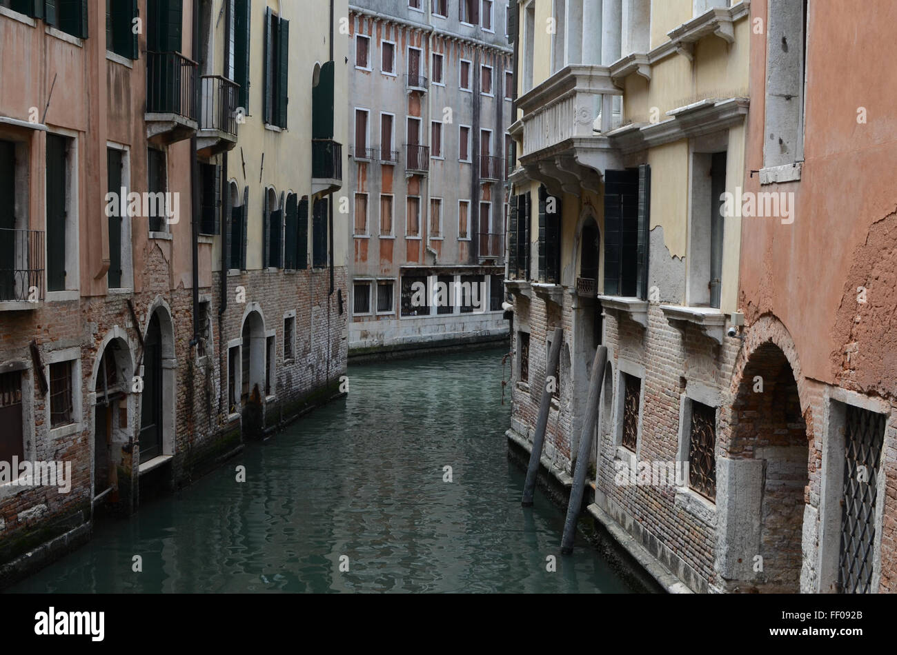 A canal runs through a narrow space between buildings, with brick walls ...