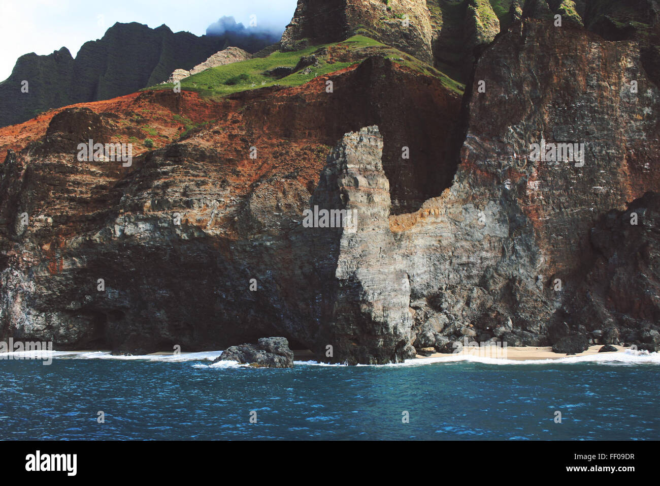 A scenic cliff rises above an oceanside beach, with waves crashing ...