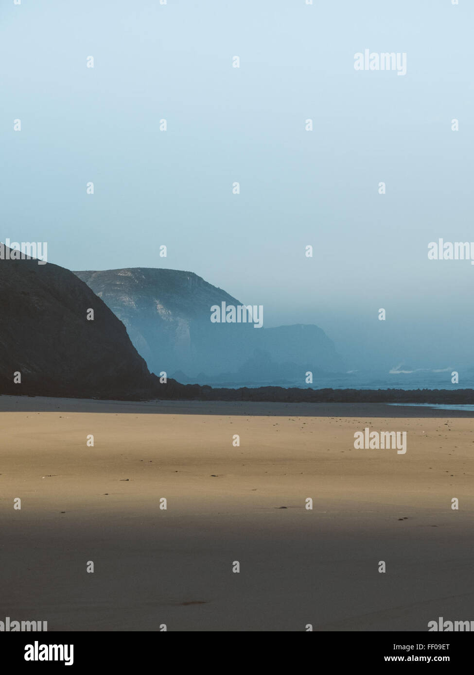 A sandy beach with rock outcrops along the shore, creating a rugged yet ...