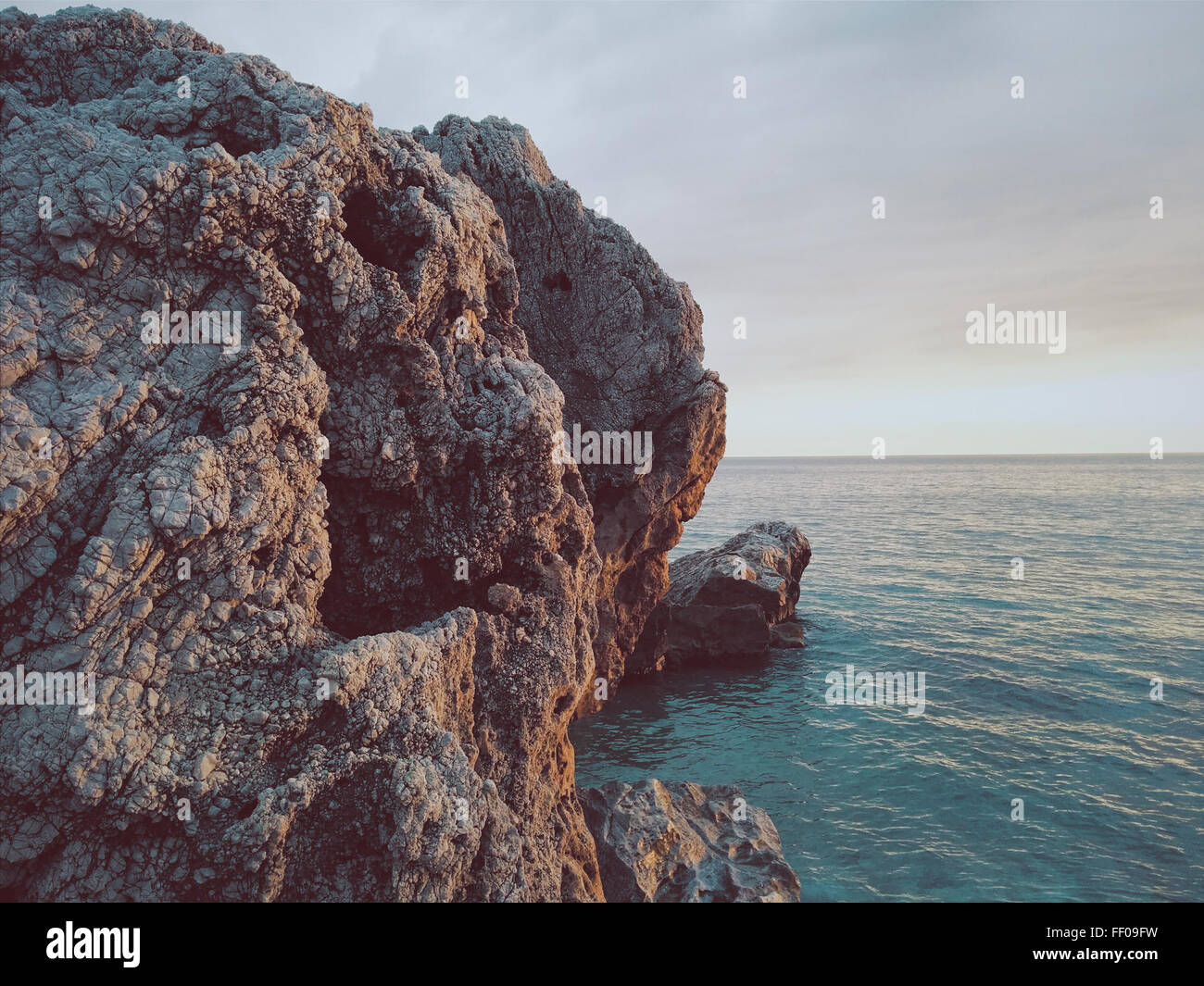 A rock formation stands at the edge of the ocean, partially reflecting ...