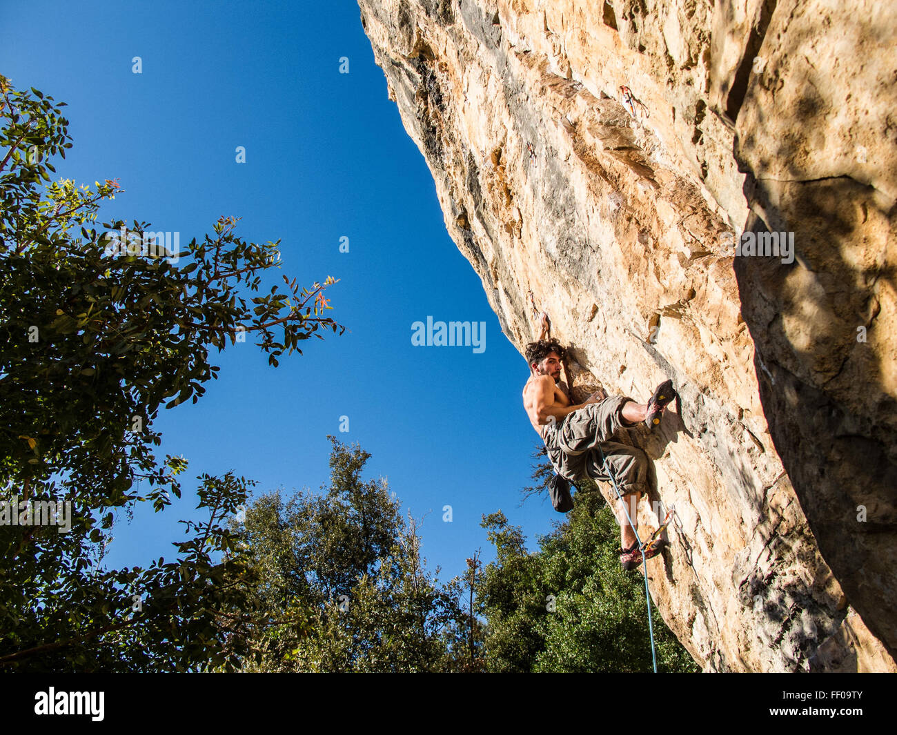 A male rock climber in action, scaling a cliff face with sunlight ...