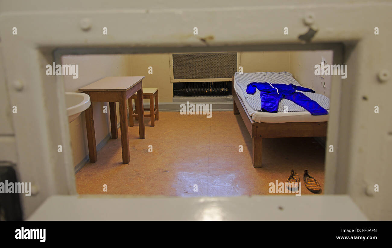 Cell with bed with blue pyjama's, little table, stool and washbasin ...