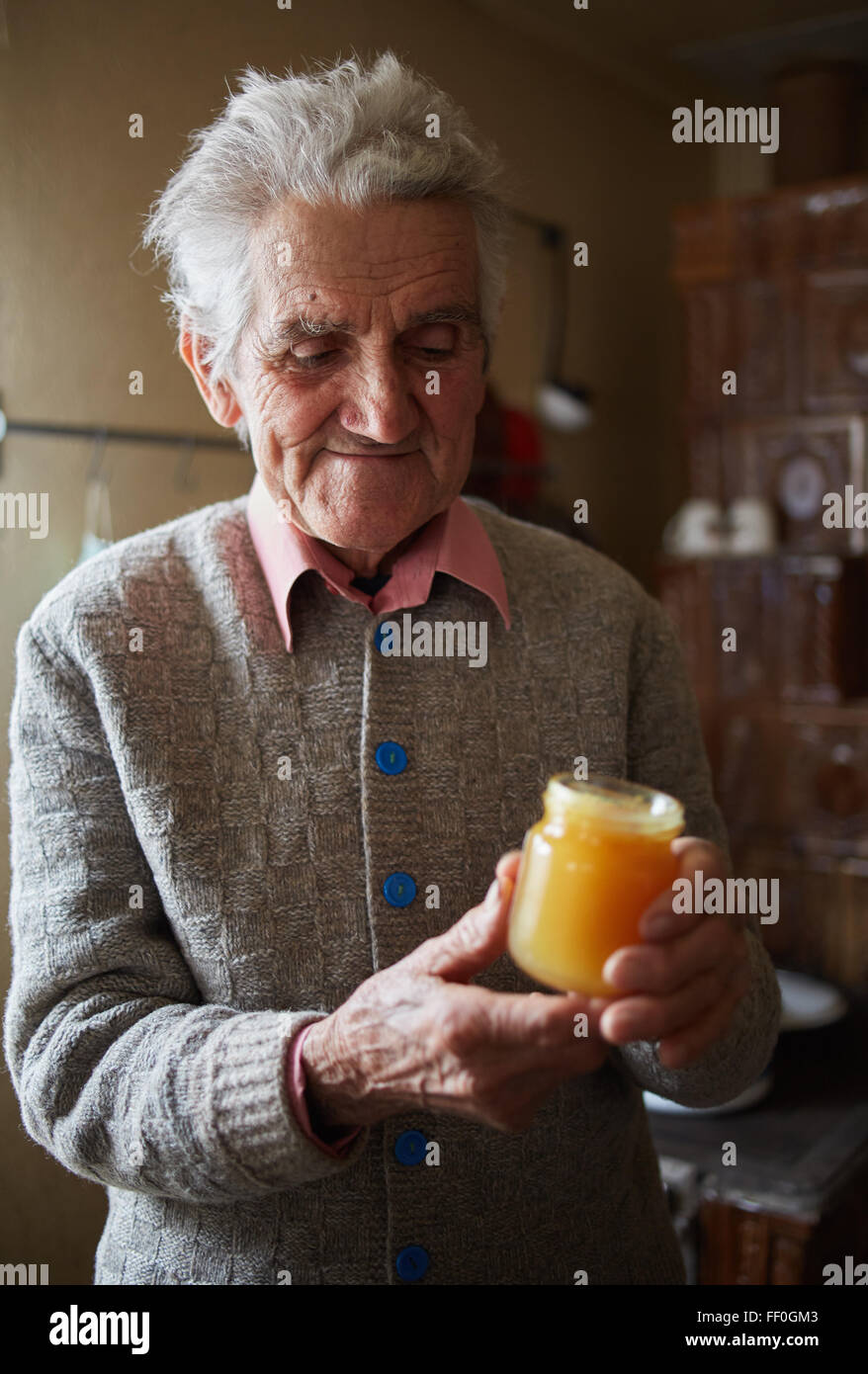 Old man indoor holding happy a jar of honey with pollen Stock Photo - Alamy