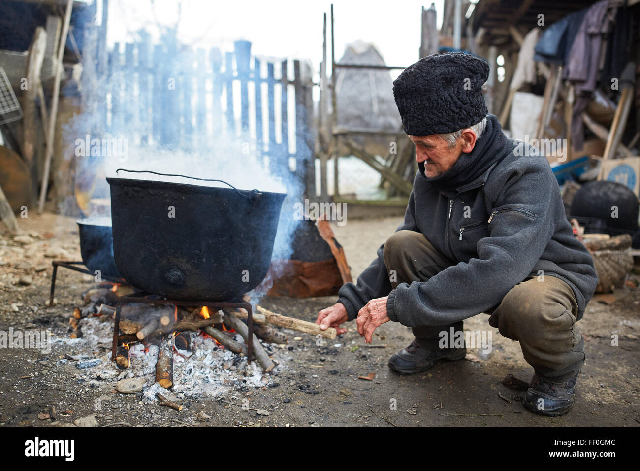 Old man putting wood on fire below large boiling cast iron pots Stock ...